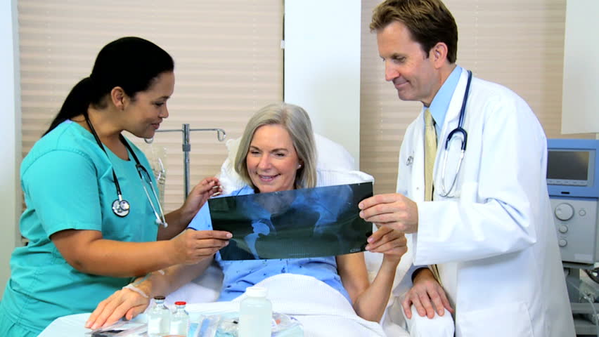 One Male And One Female Nurse Attend To An Elderly Male Patient. In The ...
