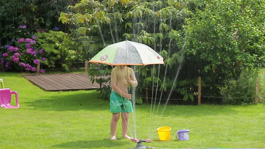 Little Boy Playing With Garden Sprinkler And Umbrella In The Backyard ...