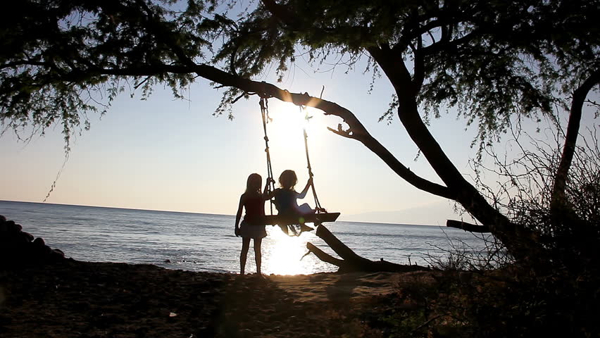 Two Sisters Play On A Rope Swing Together As The Sun Sets. Wide Shot ...