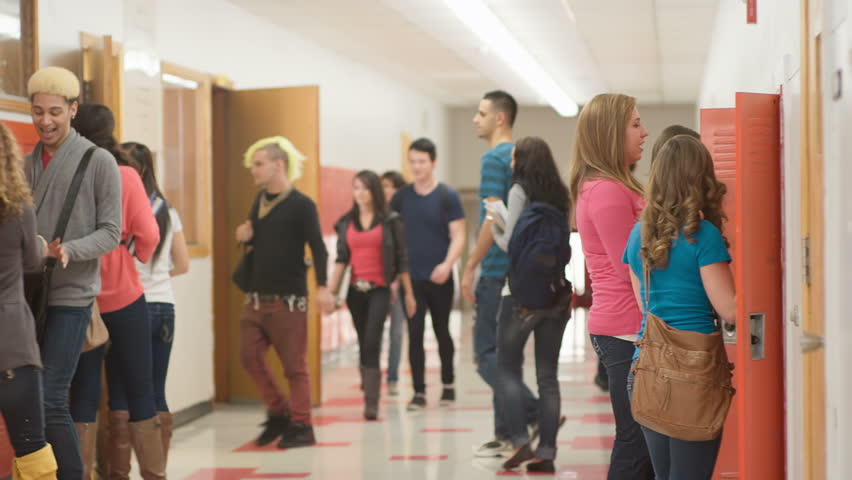 A Male Teacher Stands In A Busy Hallway With Students And Smiles Into ...